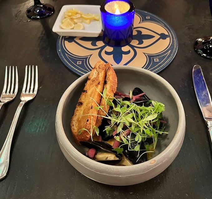 A rustic bowl of mussels arrives like buried treasure, accompanied by crusty bread perfect for soaking up the savory broth.