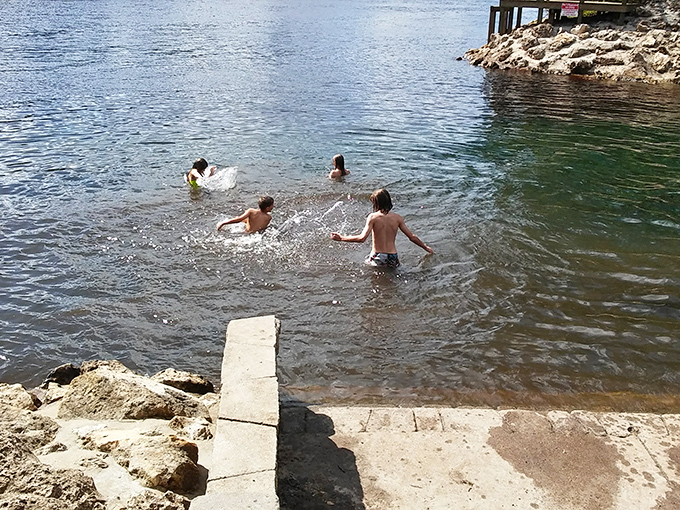 Childhood summers distilled into their purest form: kids splashing in crystal-clear waters while parents watch from limestone perches.