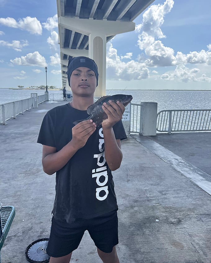 A young angler displays his catch beneath the bridge, proving life goes on above the infamous Dead Zone.