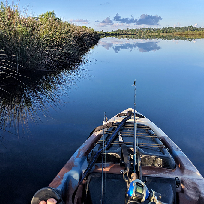 Dawn breaks over still waters as an angler's perspective captures the perfect fishing spot where patience meets possibility.