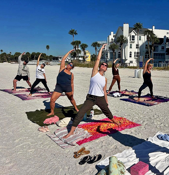 A diverse group stretches in unison on beach towels and mats, proving that beach yoga welcomes all bodies while palm trees sway like nature's own participants.
