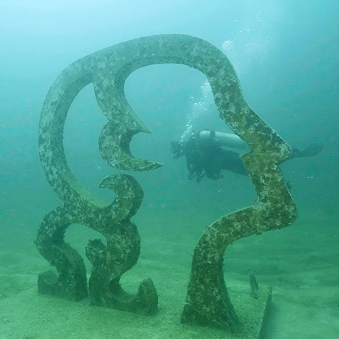 This face sculpture seems to emerge from the seafloor itself, as if the ocean is dreaming of human connection.