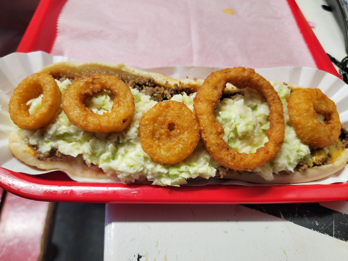 Crispy onion rings crown this loaded dog, creating a textural masterpiece that demands to be photographed before the first bite.