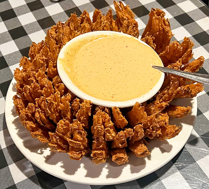The Onion Crown arrives like edible architecture, golden-fried onion strips arranged around a dipping sauce that demands investigation.