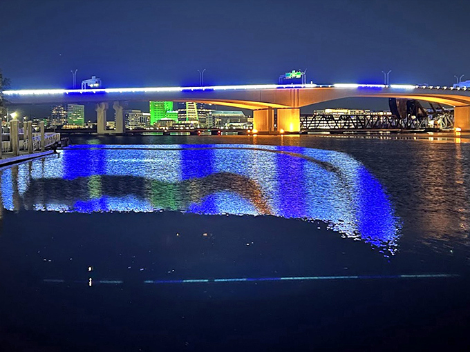 As darkness falls, Jacksonville's bridges transform into ribbons of light, reflecting their colorful glow across the river's gentle surface.