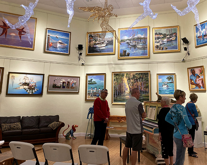 Art enthusiasts admire maritime-themed paintings while suspended decorative elements create the sensation of being underwater in this immersive gallery space.