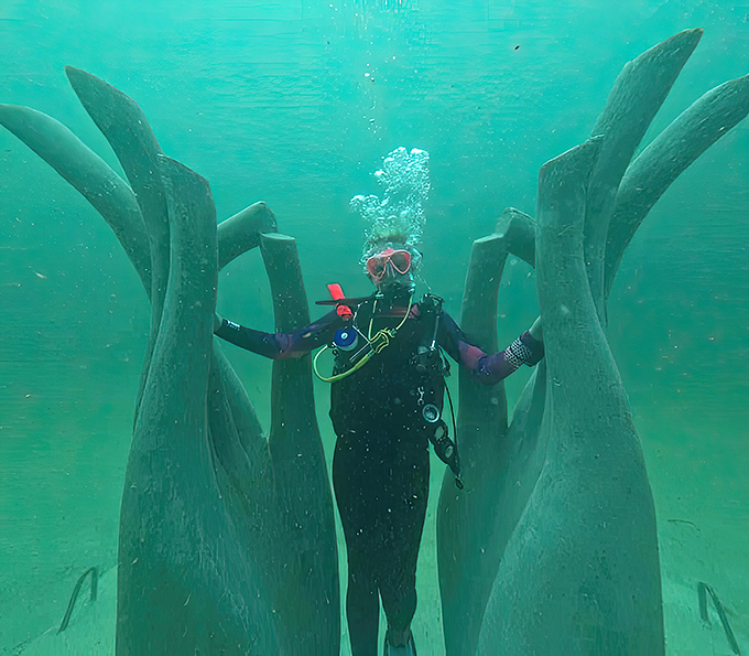 A diver finds themselves surrounded by towering sculptures that reach upward like strange underwater plants seeking sunlight.