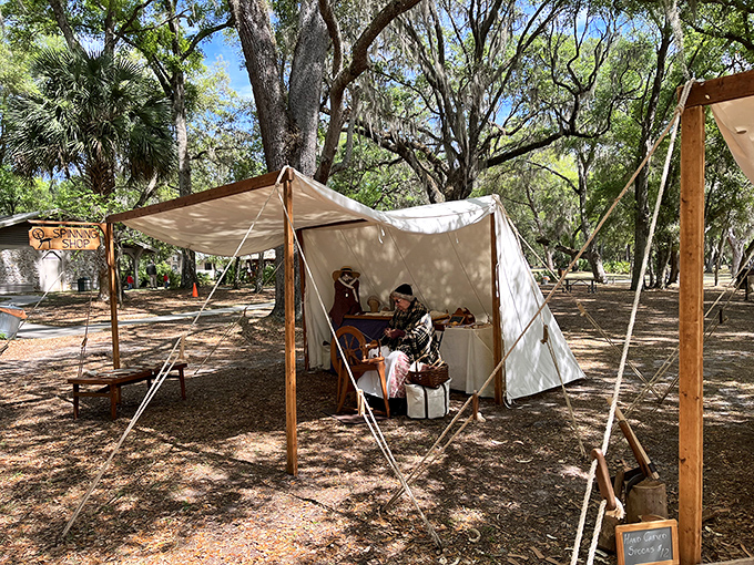 A craftsman demonstrates traditional woodworking under canvas, his skilled hands connecting modern visitors to forgotten frontier arts.
