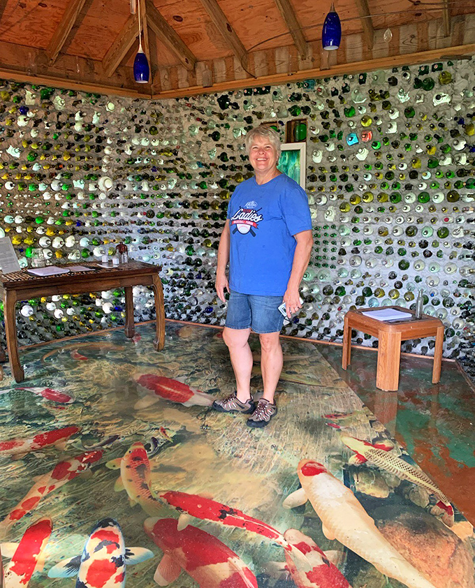 A visitor stands amazed on the 3D epoxy floor that creates the illusion of koi fish swimming beneath their feet, surrounded by walls of glimmering bottle ends.