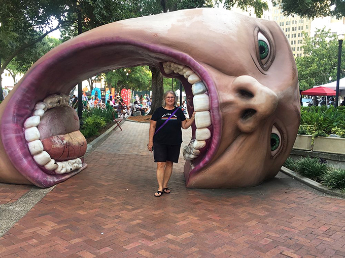 Visitors pose with the giant head sculpture, proving that sometimes the best vacation photos involve pretending to be eaten by inanimate objects.