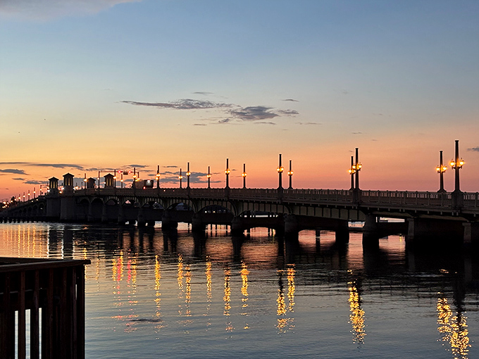 As darkness falls, the bridge transforms into a string of pearls across the water, each light creating its own reflection.