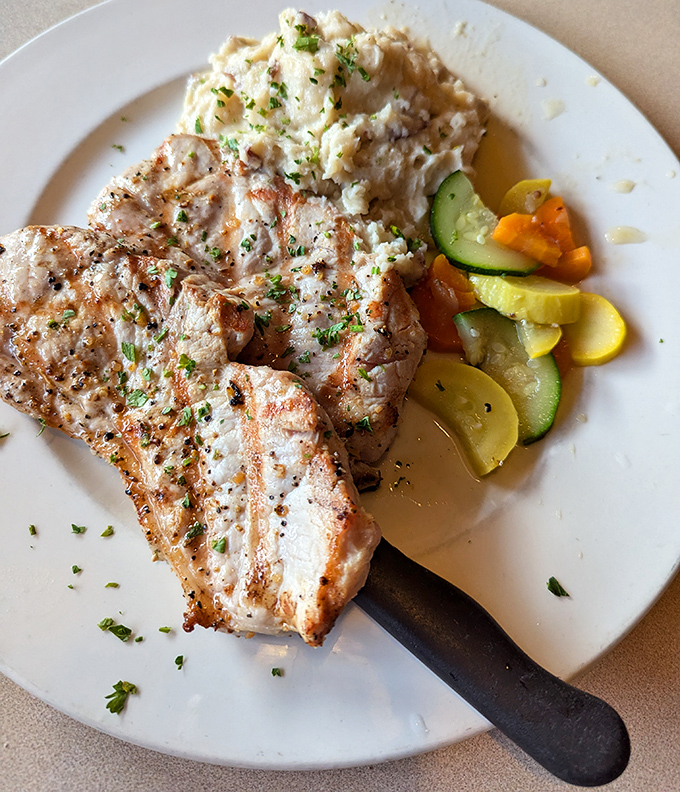 Pork chops grilled to juicy perfection share the plate with garden-fresh vegetables and cloud-like mashed potatoes &ndash; comfort food elevated to art form.