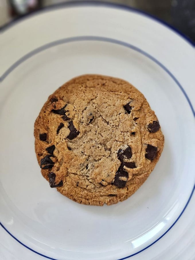 A chocolate chip cookie sits in perfect simplicity on a white plate, promising homestyle comfort in every bite.