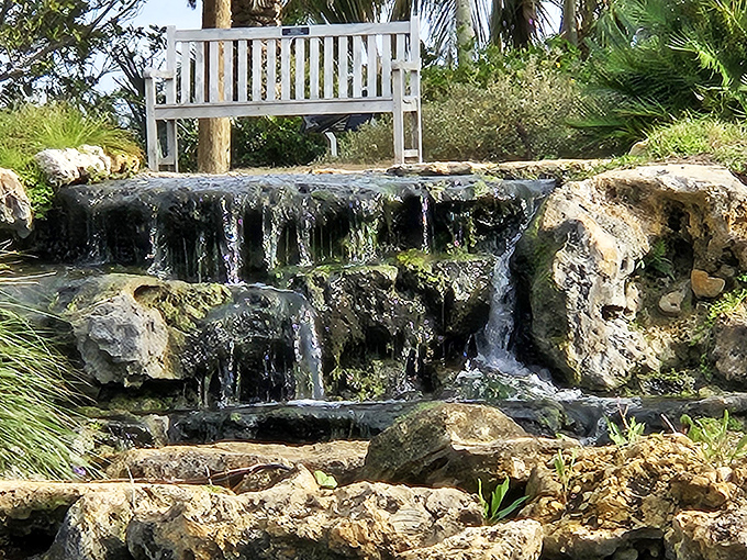A different angle of Naples Garden's waterfall reveals its artistic stone arrangement. Water flows like liquid silver over carefully placed rocks.