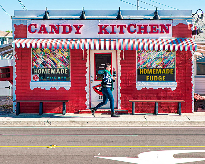 The cherry-red exterior of Candy Kitchen stands like a beacon of childhood joy, complete with classic striped awning and nostalgic charm.