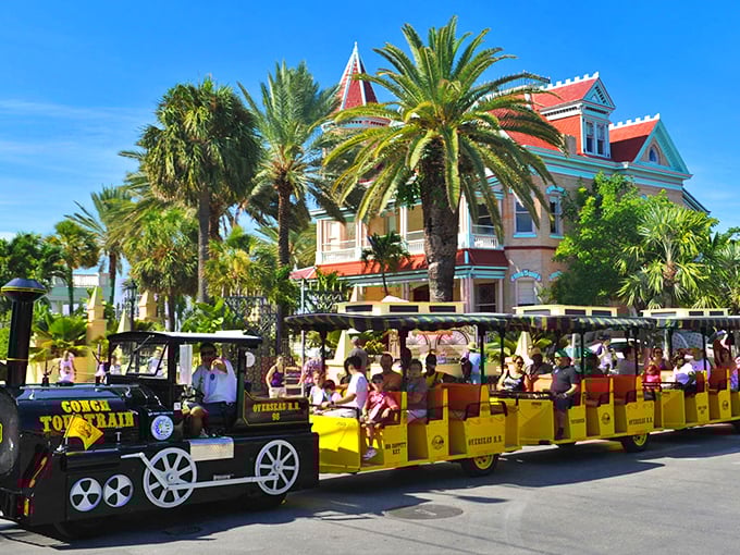 The iconic yellow Conch Tour Train glides past palm trees and historic buildings, a moving postcard of Key West's tropical charm.