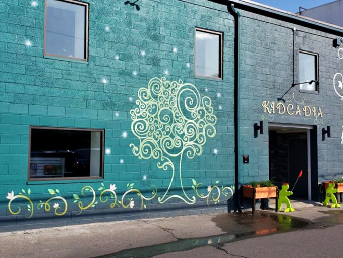 The whimsical turquoise exterior of Kydcadia beckons with its enchanting tree design, promising magical adventures before you even step inside.