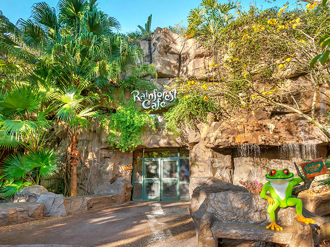 The Rainforest Cafe entrance beckons with lush foliage and rocky facades, a green oasis promising adventure before you've even checked the menu.