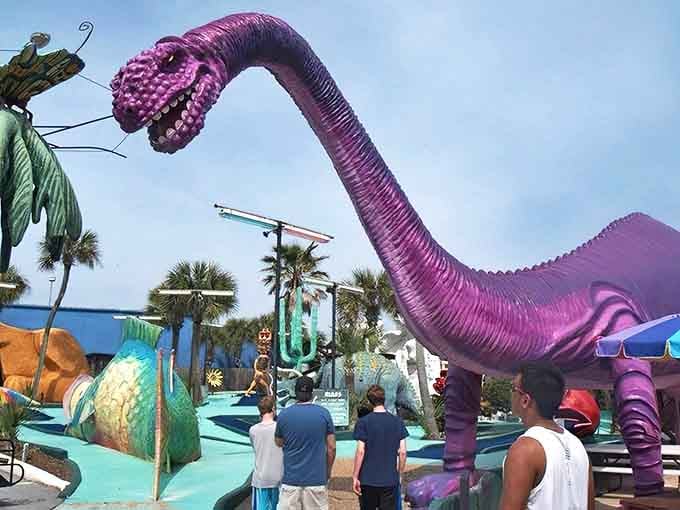A towering purple brontosaurus welcomes mini-golfers with a toothy grin, standing guard over the whimsical world of Goofy Golf in Panama City Beach.