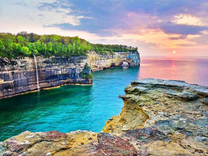 Nature's masterpiece unfolds at Pictured Rocks, where Lake Superior's turquoise waters meet towering sandstone cliffs painted with mineral streaks.