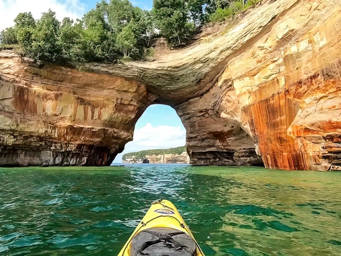 Nature's gateway beckons as sunlight streams through this magnificent rock arch, creating a portal to Lake Superior's endless blue horizon.
