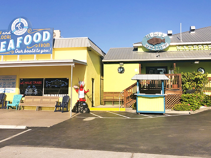 The cheerful yellow and seafoam-green exterior of Rusty Bellies welcomes seafood lovers with a giant red lobster standing guard, promising fresh-caught delights within.
