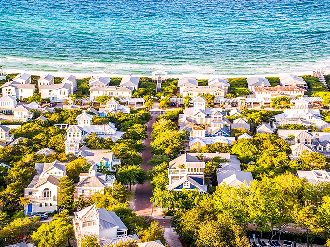 Seaside's iconic pastel cottages line up like colorful soldiers, standing guard between lush greenery and the emerald Gulf waters beyond.