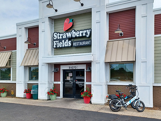 The welcoming facade of Strawberry Fields Restaurant beckons with its cheerful red accents and iconic strawberry logo, promising a magical culinary journey inside.