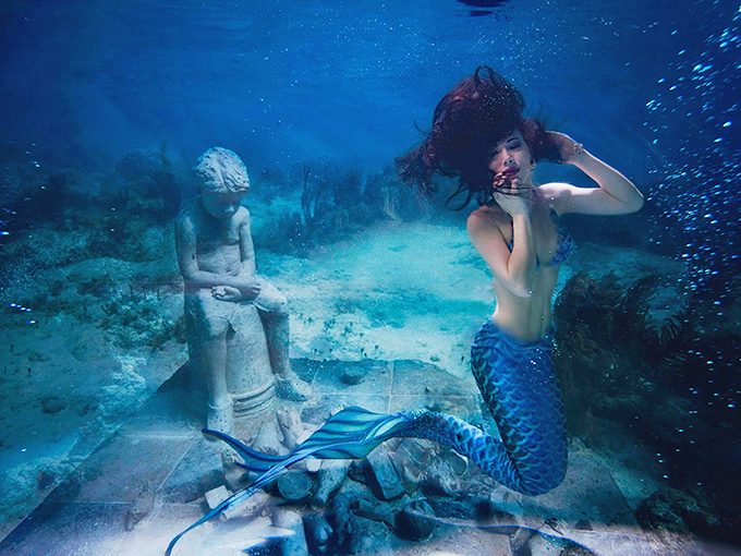 Underwater magic unfolds as a performer glides past ancient statues in Weeki Wachee's crystal-clear spring, creating a dreamlike scene that captivates audiences of all ages.