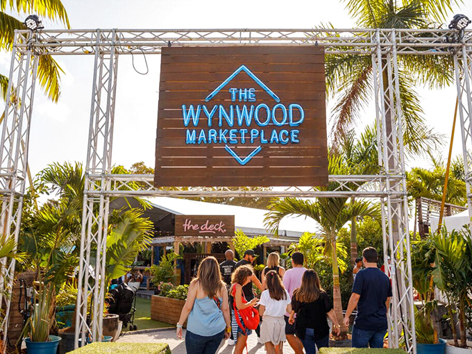 The iconic Wynwood Marketplace entrance welcomes visitors with its distinctive blue neon sign, promising a feast for all senses beyond those wooden gates.