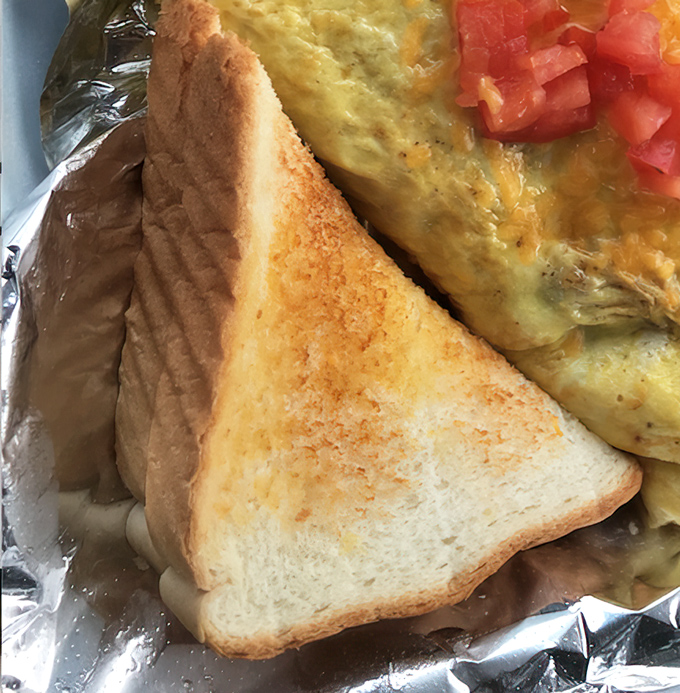 Golden-brown toast frames this breakfast masterpiece, where eggs and bacon perform their timeless morning duet on a cheerful sun-patterned plate.