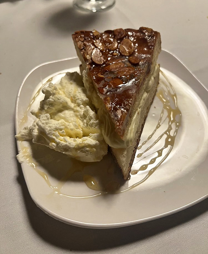 A slice of heaven featuring honey-infused cheesecake topped with caramelized almonds, served alongside a cloud of freshly whipped cream.