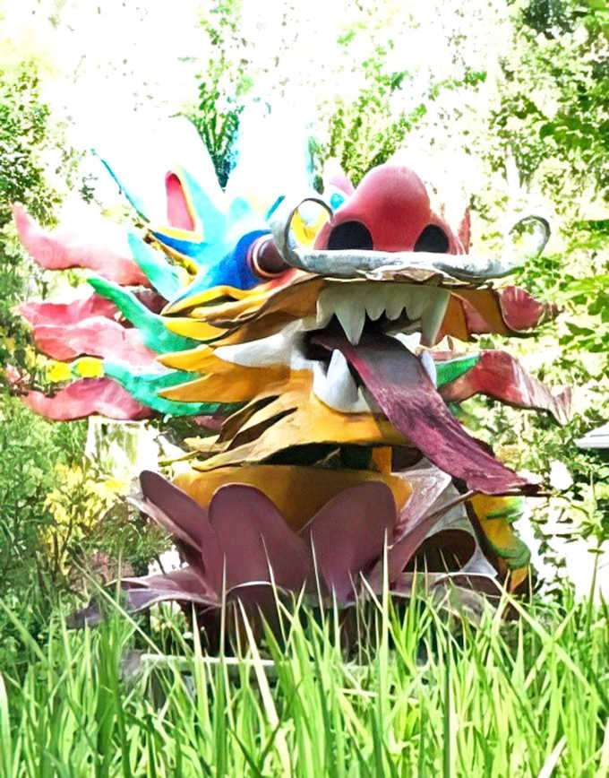 A colorful dragon sculpture emerges from the grass, part of an ever-changing outdoor gallery of handcrafted curiosities.