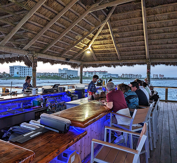 As evening falls, the bar glows with blue light and possibility, bartenders crafting drinks with the casual expertise of people who know they've got the best office view.