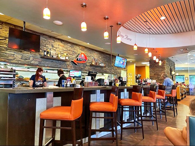 The counter seating offers front-row tickets to the culinary show, where orange chairs pop against stone walls and breakfast magic happens.