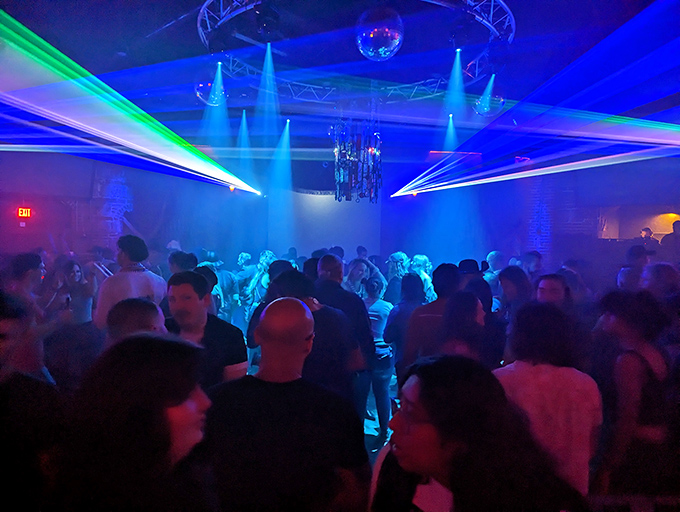 The dance floor transforms into a sea of moving bodies as green and blue lasers create geometric patterns overhead, the beating heart of The Castle's nightlife.