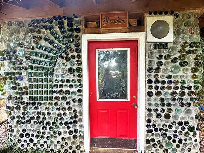 A cheerful red door framed by bottle-embedded walls invites visitors to step into a world where ordinary objects become extraordinary.