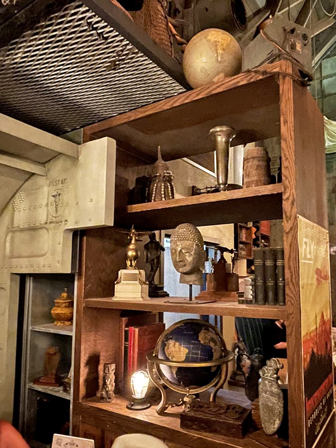 Every shelf tells a story of fictional expeditions, with vintage globes, Buddha heads, and weathered books creating a museum you can eat in.