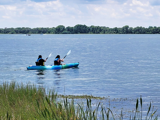 Two kayakers paddle across open waters where the canal meets the lake, experiencing the dramatic transition from enclosed waterway to expansive horizon.