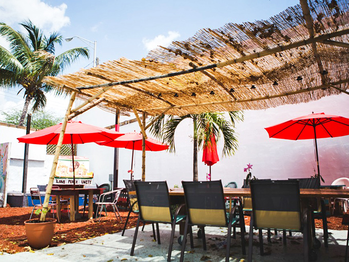 Red umbrellas stand guard over wooden tables where strangers become friends, united by the universal language of good food.