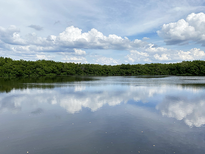 Mirror-like waters perfectly reflect puffy white clouds, creating an optical illusion where sky and water become indistinguishable.
