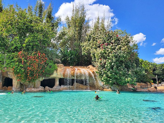 Waterfalls cascade over natural rock formations, creating a tropical soundtrack for swimmers enjoying this sun-drenched aquatic playground.