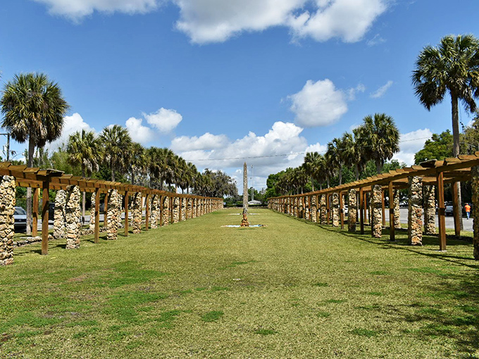 Two rows of stone columns create a dramatic perspective, drawing the eye toward the garden's centerpiece while palm trees stand sentinel.