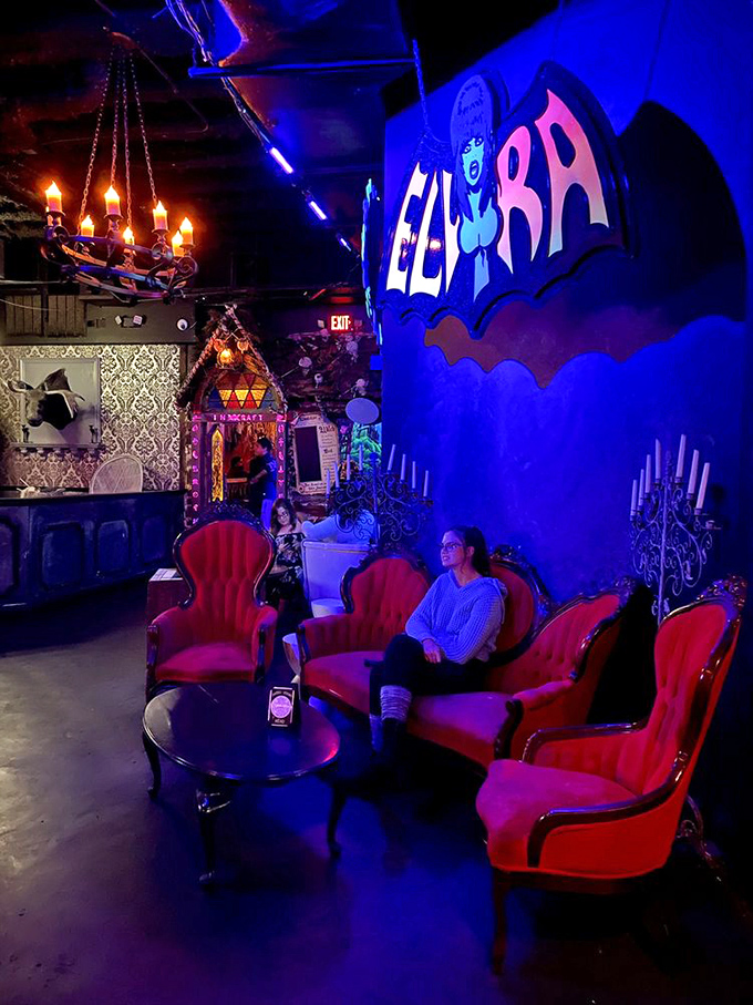 Plush red Victorian chairs create intimate seating areas beneath the watchful gaze of Elvira, perfect for plotting world domination or just enjoying your spectacularly spooky cocktail.