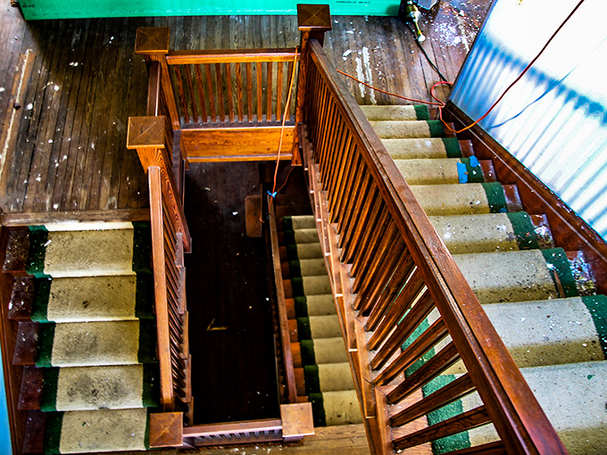 The staircase spirals downward like a wooden waterfall, its craftsmanship a testament to an era when homes were built to outlast lifetimes.