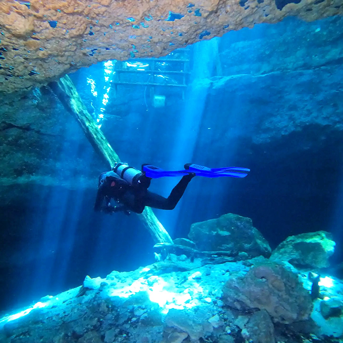 Sunbeams pierce the water like nature's own spotlight system, illuminating a diver exploring this liquid cathedral of limestone.