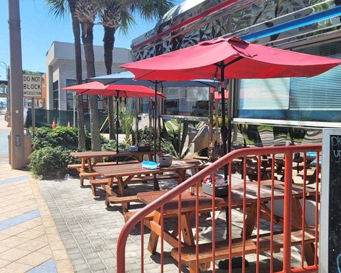 Red umbrellas shade outdoor tables where palm trees and people-watching provide the perfect backdrop for your morning coffee ritual.