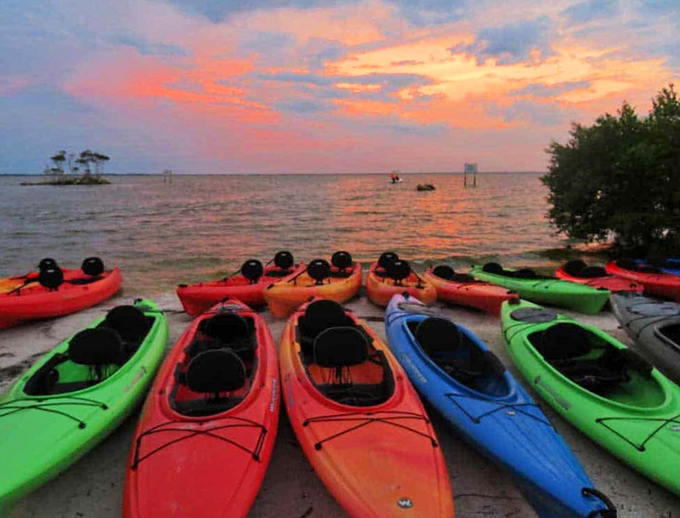Daytime preparation for nighttime magic &ndash; a rainbow of kayaks awaits adventurers against a cotton candy Florida sunset.