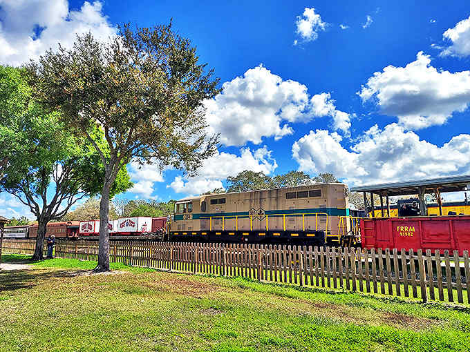 A peaceful scene of historic trains resting under Florida's dramatic sky, the white picket fence adding a touch of nostalgic Americana.