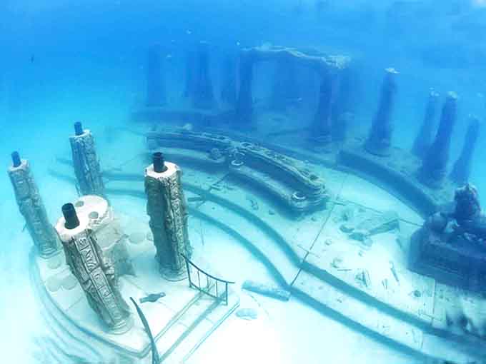 Massive columns create the illusion of an underwater temple, their imposing presence softened by the gentle movement of passing fish.